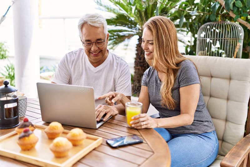 Middle Age Hispanic Couple Having Breakfast Using Laptop at the Terrace ...