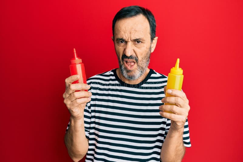 Middle Age Hispanic Man Holding Ketchup and Mustard Bottle Clueless and ...