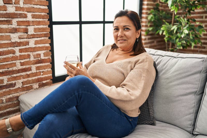 Middle Age Hispanic Woman Drinking Champagne Sitting on Sofa at Home ...