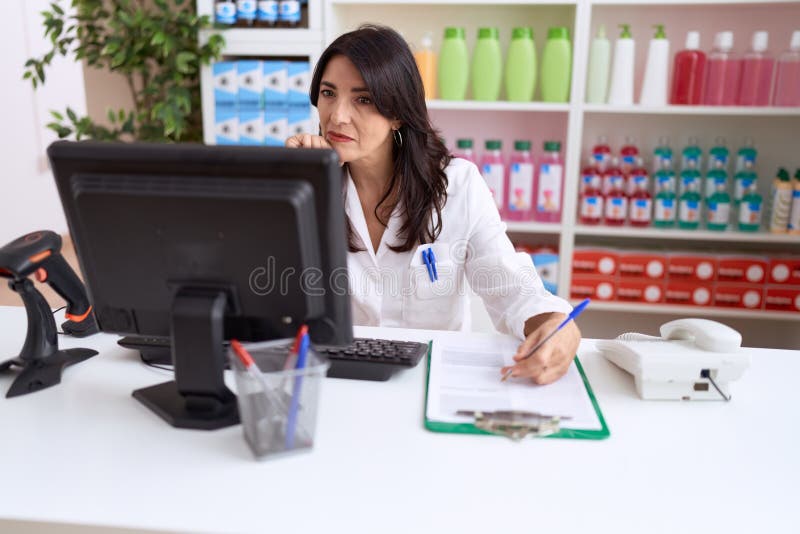 Middle Age Hispanic Woman Pharmacist Writing on Document Using Computer ...
