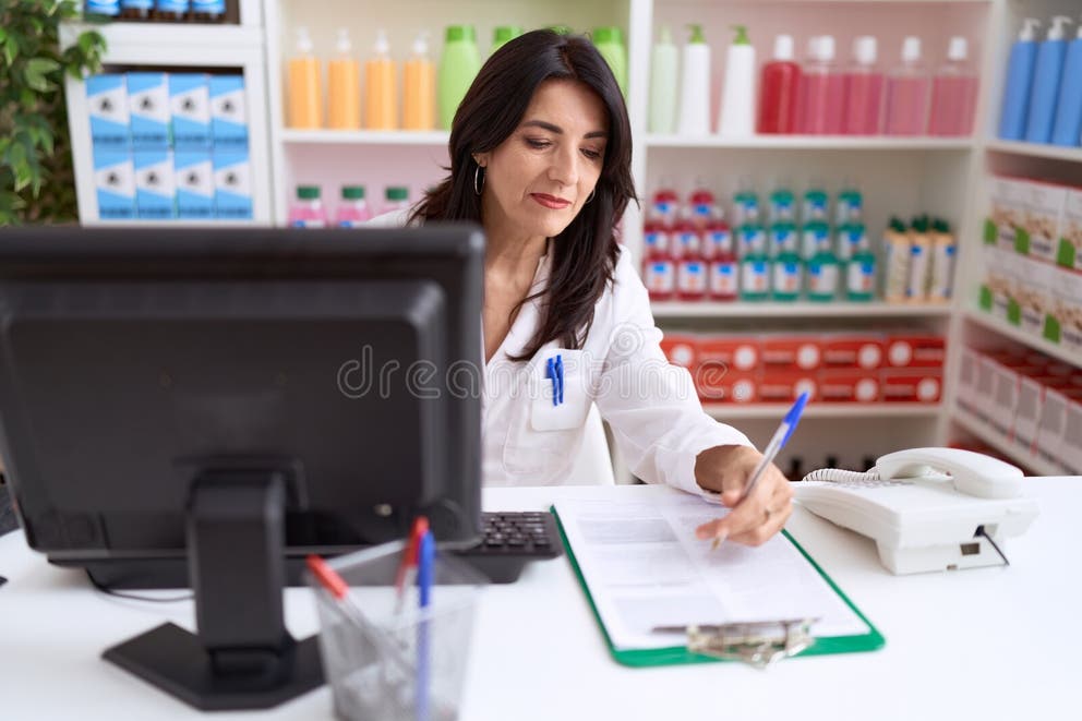Middle Age Hispanic Woman Pharmacist Writing on Document Using Computer ...