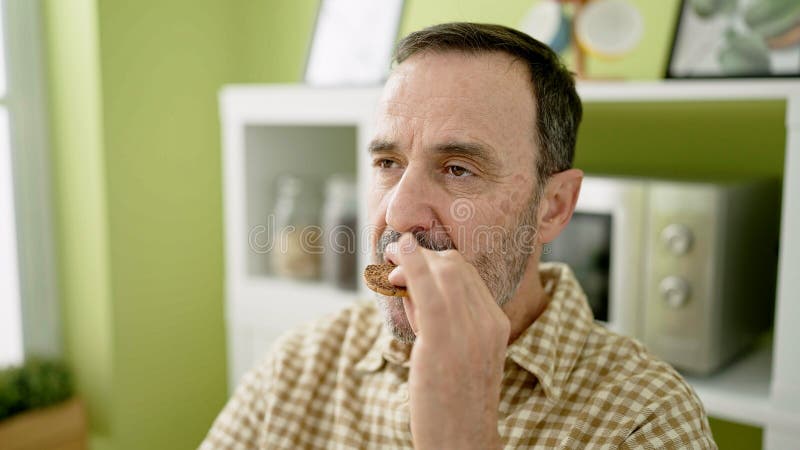 Middle Age Man Eating Cookie Sitting on Table at Home Stock Image ...