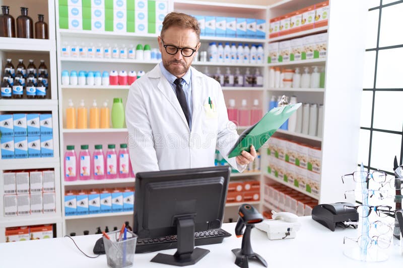 Middle Age Man Pharmacist Reading Document Using Computer at Pharmacy ...