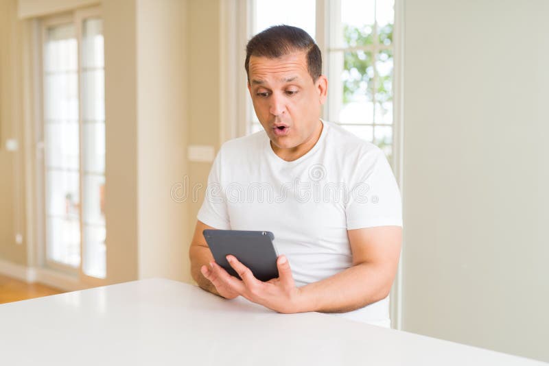 Middle Age Man Using Digital Table at Home Scared in Shock with a ...