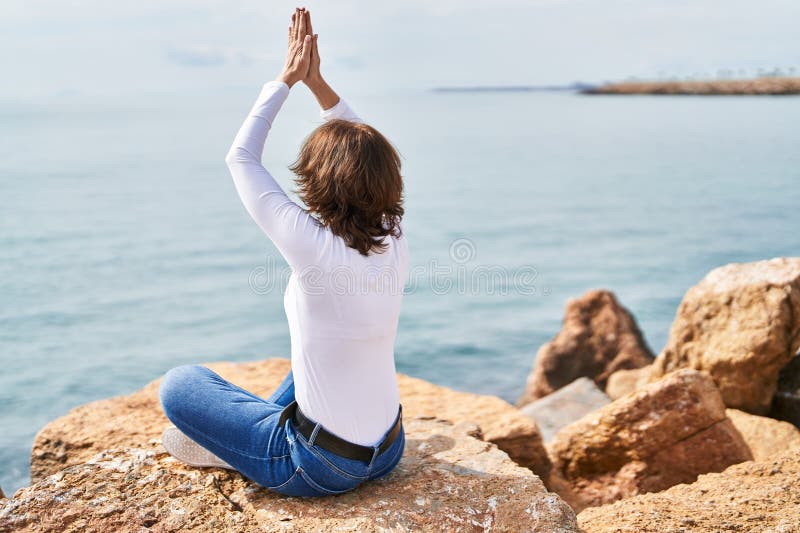 Middle Age Woman Doing Yoga Exercise Sitting on the Rock at Seaside ...
