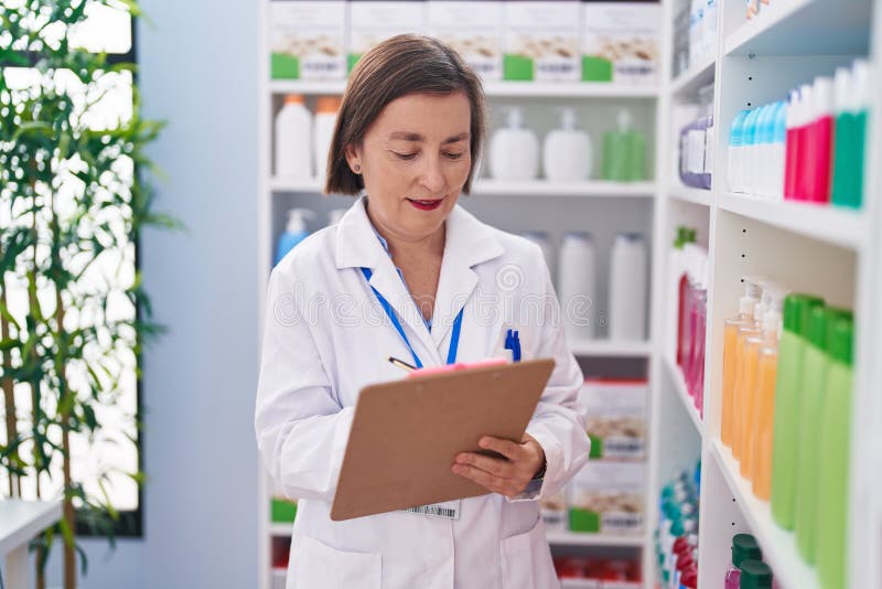 Middle Age Woman Pharmacist Writing on Document at Pharmacy Stock Image ...