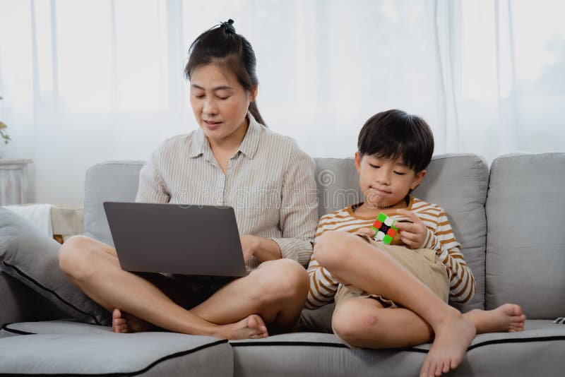 A Middle Aged Asian Single Mother Uses Her Laptop On The Sofa In Her