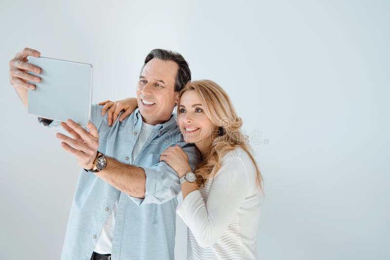 Middle Aged Couple Taking Selfie With Digital Tablet On Grey Stock