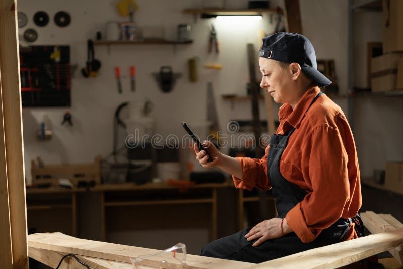 Middle-aged Female Carpenter Using Smartphone, Having a Break in ...