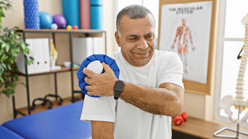 Middle-aged Hispanic Man Applying Ice Pack To Shoulder in Physiotherapy ...