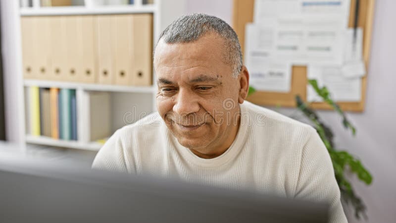 A Middle-aged Hispanic Man Smiles while Working on a Computer in a ...