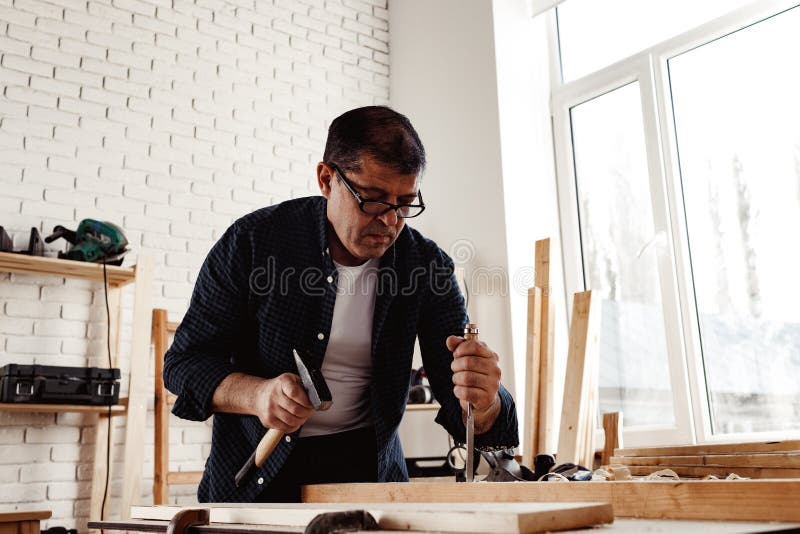 Middle-aged Man Carpenter Working in a Workshop with Chisel and Hammer ...