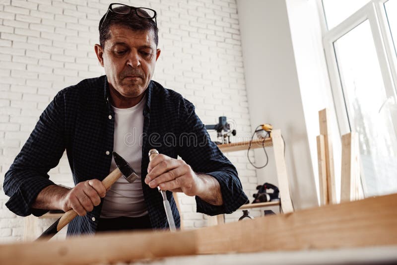 Middle-aged Man Carpenter Working in a Workshop with Chisel and Hammer ...