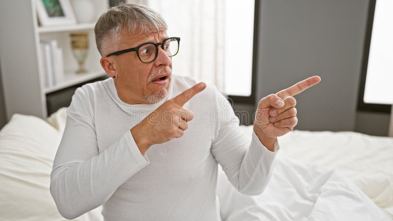 Middle-aged Man in Glasses, Pointing Excitedly while Sitting on the Bed ...