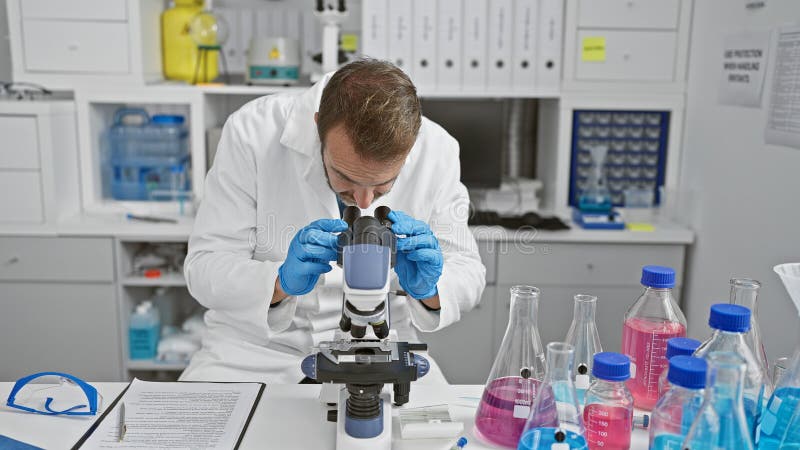 Middle-aged Man in Lab Coat Using a Microscope Surrounded by Scientific ...