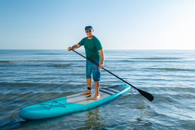 A Man In Shorts Stands On A Sup Board In The Evening At Sunset In The