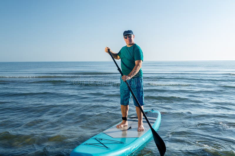 A Man In Shorts Stands On A Sup Board In The Evening At Sunset In The