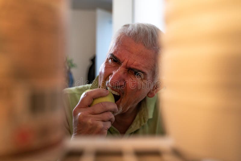 Middle-aged Single Man Biting into an Apple from the Refrigerator ...