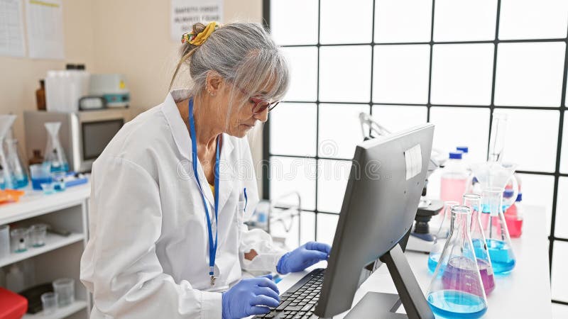 A Middle-aged Woman Scientist in a Lab Coat Working on a Computer in a ...