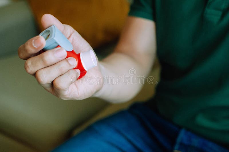 A Young Man is Holding an Asthma Inhaler Device while Sitting on a ...