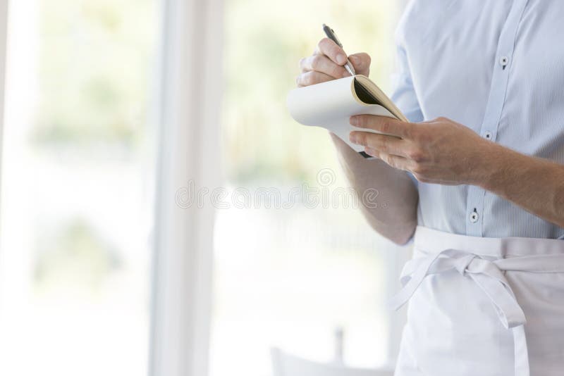 Midsection of Young Waiter Writing on Notepad while Standing at ...