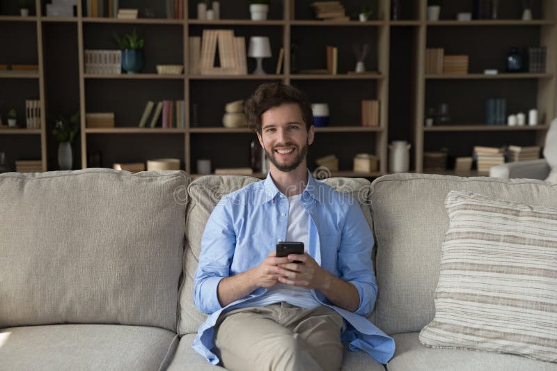 Millennial Guy Sit on Couch Hold Smartphone Look at Camera Stock Image ...