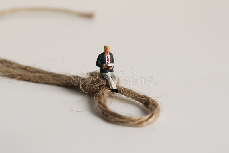 A Miniature Man Sitting on a Strapped Rope and Reading. Stock Image ...