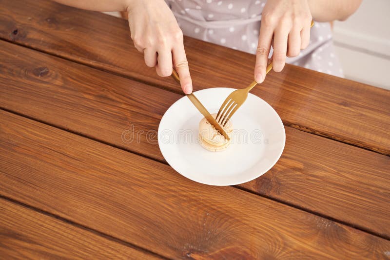Minimalist Dining: Hands Cutting Macaron with Fork and Knife on Wooden ...