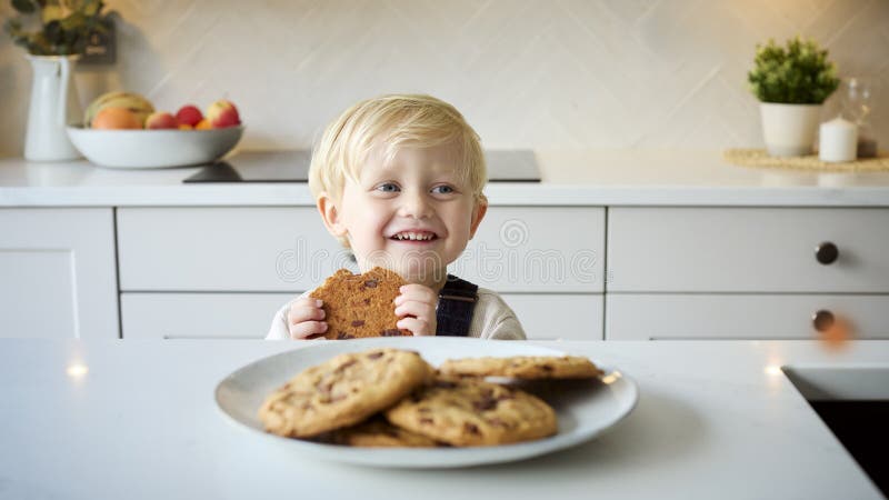 Mischievous Young Boy Eating Giant Cookie from Plate in Kitchen at Home ...