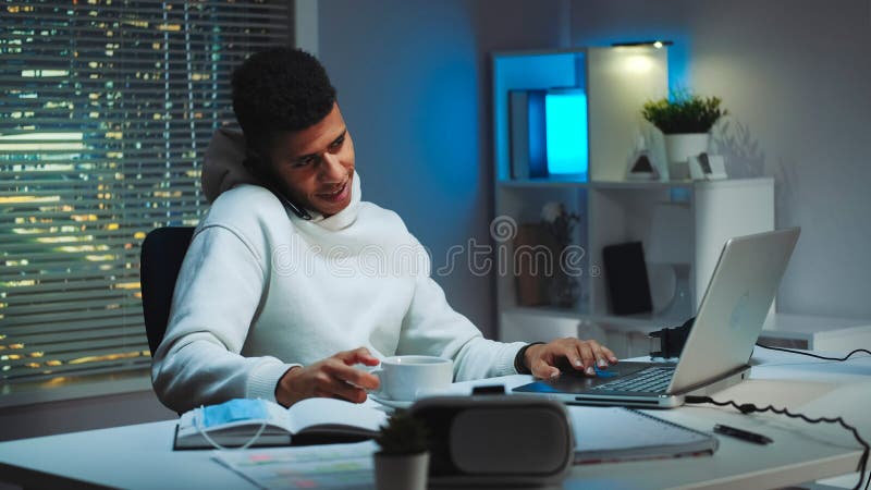 Mixed-race Man Working on Computer, Speaking by Smartphone and Drinking ...