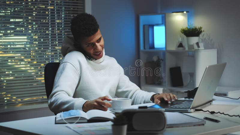 Mixed-race Man Working on Computer, Speaking by Smartphone and Drinking ...