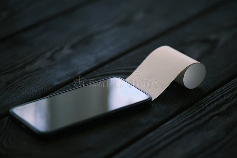 A Mobile Phone with a Blank Check from it on Black Wooden Table Stock ...