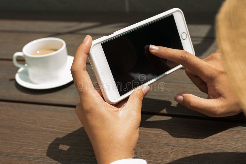 Mockup Image of Hands Holding Black Mobile Under the Sun at Coffee Shop ...