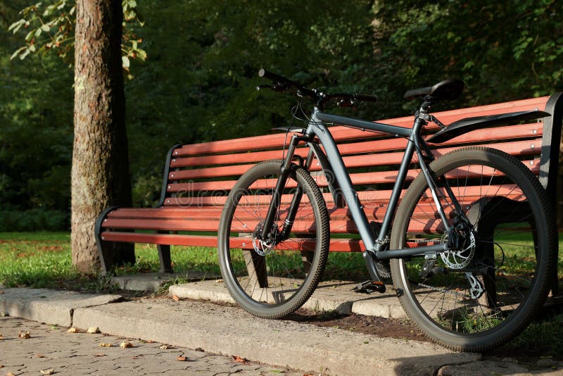 Modern Bicycle Near Wooden Bench Outdoors, Space for Text Stock Photo ...
