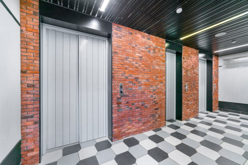 A Modern Elevator Lobby with Three Elevator Doors Set in a Brick Wal ...