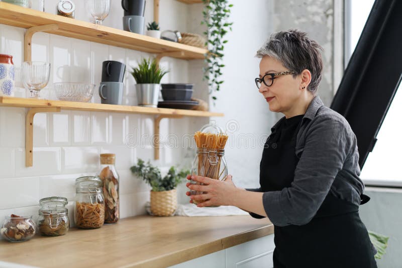 Modern Grandmother is Preparing Dinner in the Kitchen, Holding ...