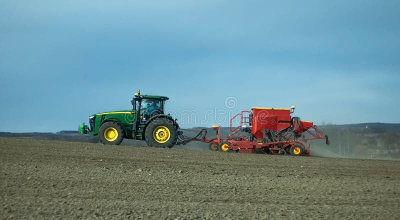 Modern Green Tractor Pulling a Red Seed Drill in the Back on a Farm in ...