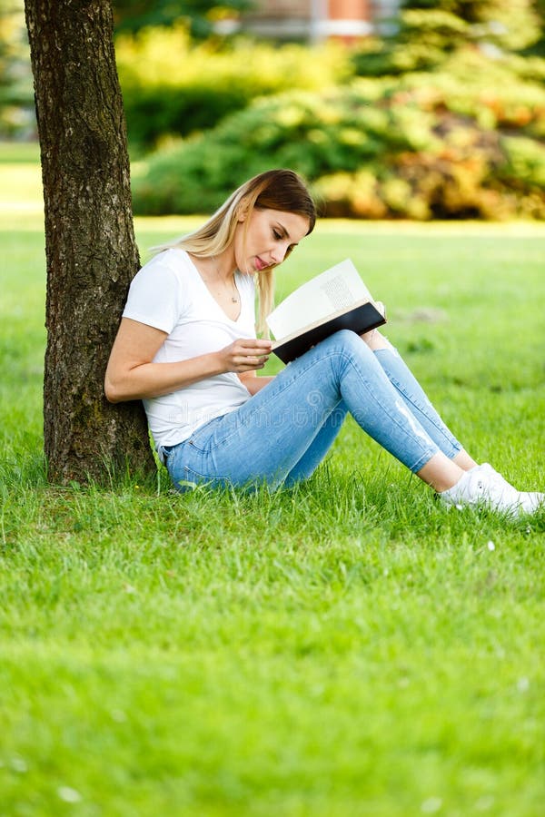 Modern Student Sitting in Park Under the Tree and Reading the Bo Stock ...