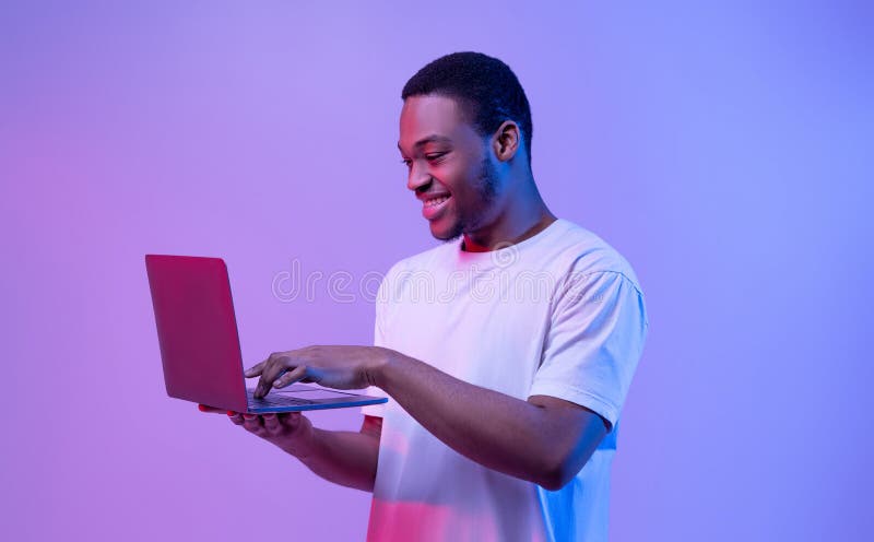 Modern Technologies. Happy Black Man Using Laptop Computer in Neon ...