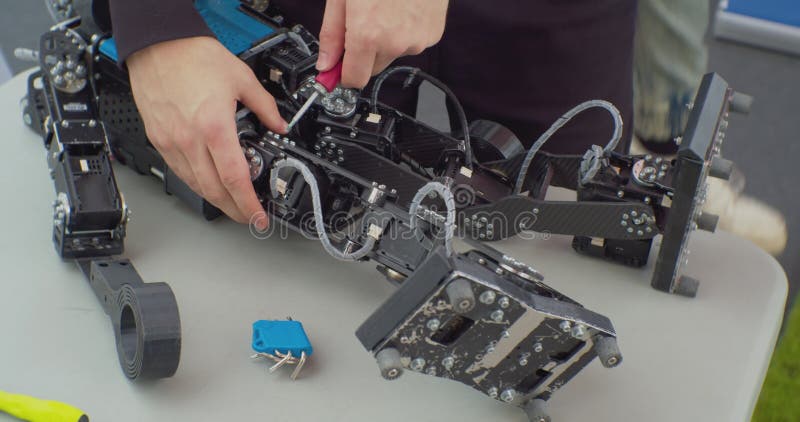 Mechanical Assembly of a Small Robot on Wheels Using a Screwdriver. Hands of a Working Man Close ...