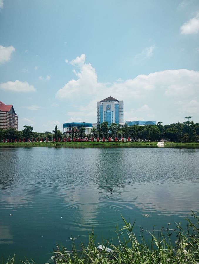Modern University Building Reflected in a Calm Lake Under a Bright Blue ...