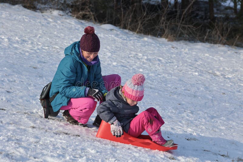 Mom Helps Daughter Get on Bobsleigh while Sledding in the Snow Stock ...