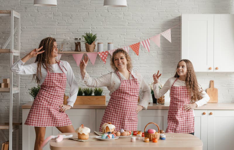Mom And Her Daughter Girls Are Dancing In The Kitchen In Aprons