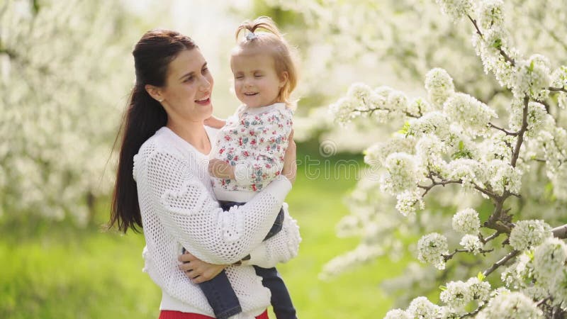 Mom Spinning With A Daughter In Her Arms In The Park By A Flowering