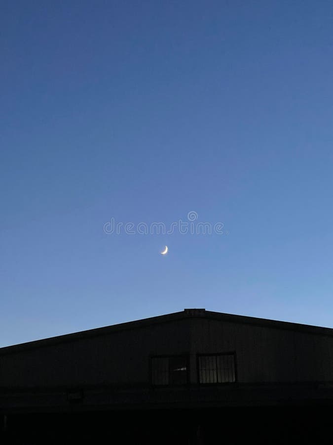 The Moon in a Clear Sky Behind a Building with Some Windows Stock Photo ...