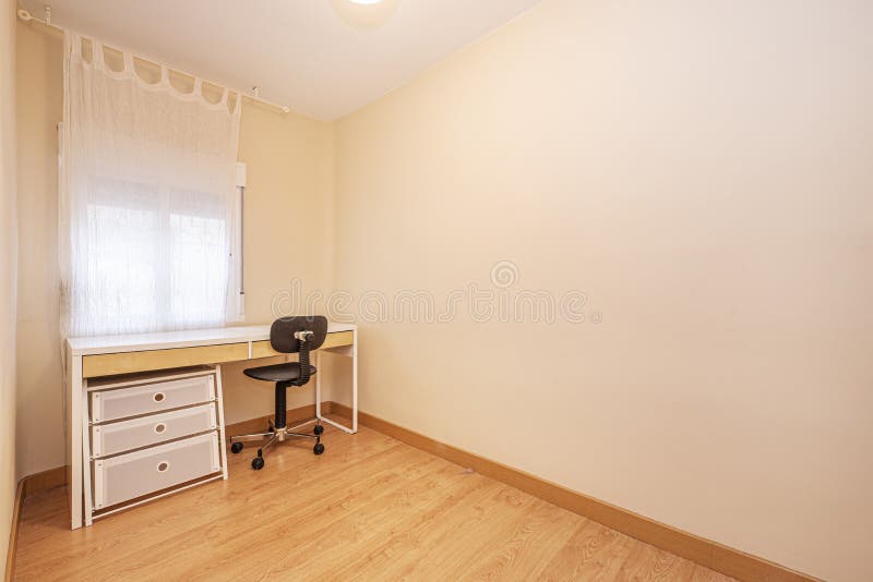 A Mostly Empty Room with a White Study Table with a Chest of Drawers ...