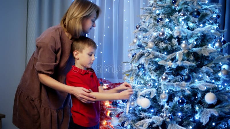 A Mother Helps Her Son Hang Christmas Decorations on the Tree. Stock ... A Mother Helps Her Son Hang Christmas Decorations on the Tree. Stock ...