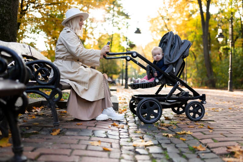 Mother Sitting on a Bench and Rocking the Baby in a Stroller. Stock ...