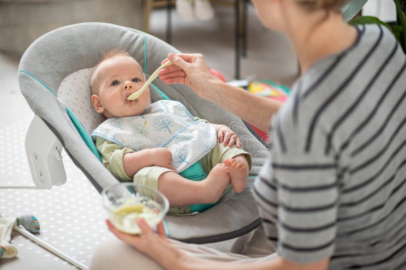 Mother Spoon Feeding Her Baby Boy Infant Child in Baby Chair with Fruit ... Mother Spoon Feeding Her Baby Boy Infant Child in Baby Chair with Fruit ...