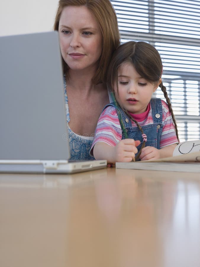 Mother Using Laptop While Daughter Coloring At Table Stock Photo ...